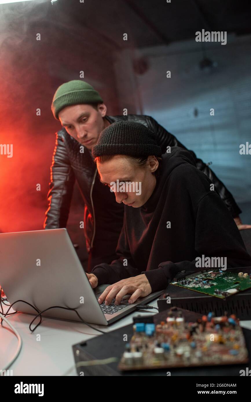 Two men bending over laptop in the darkness Stock Photo - Alamy