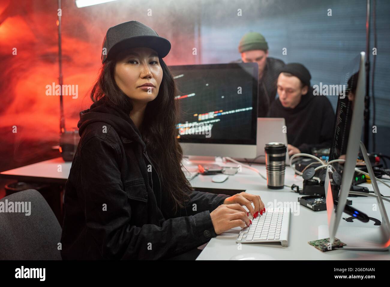 Serious female hacker sitting in front of computer against two guys ...