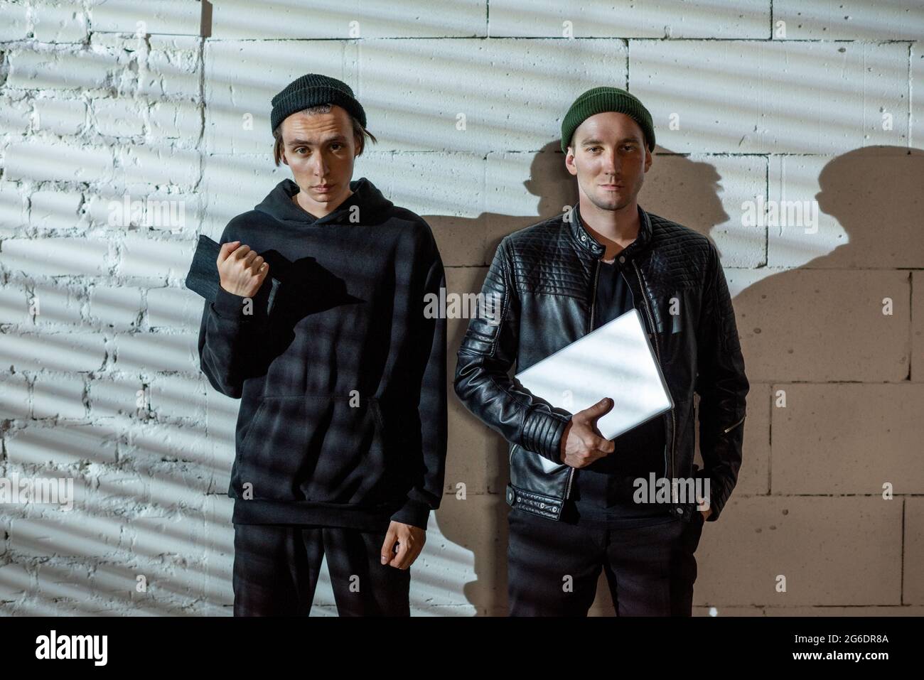 Two young male hackers standing by white painted brick wall Stock Photo ...