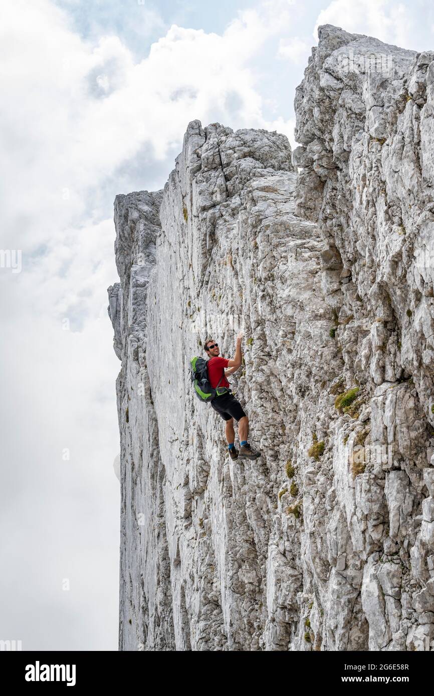 Young man climbing a vertical rock face without a rope, rocky mountains ...