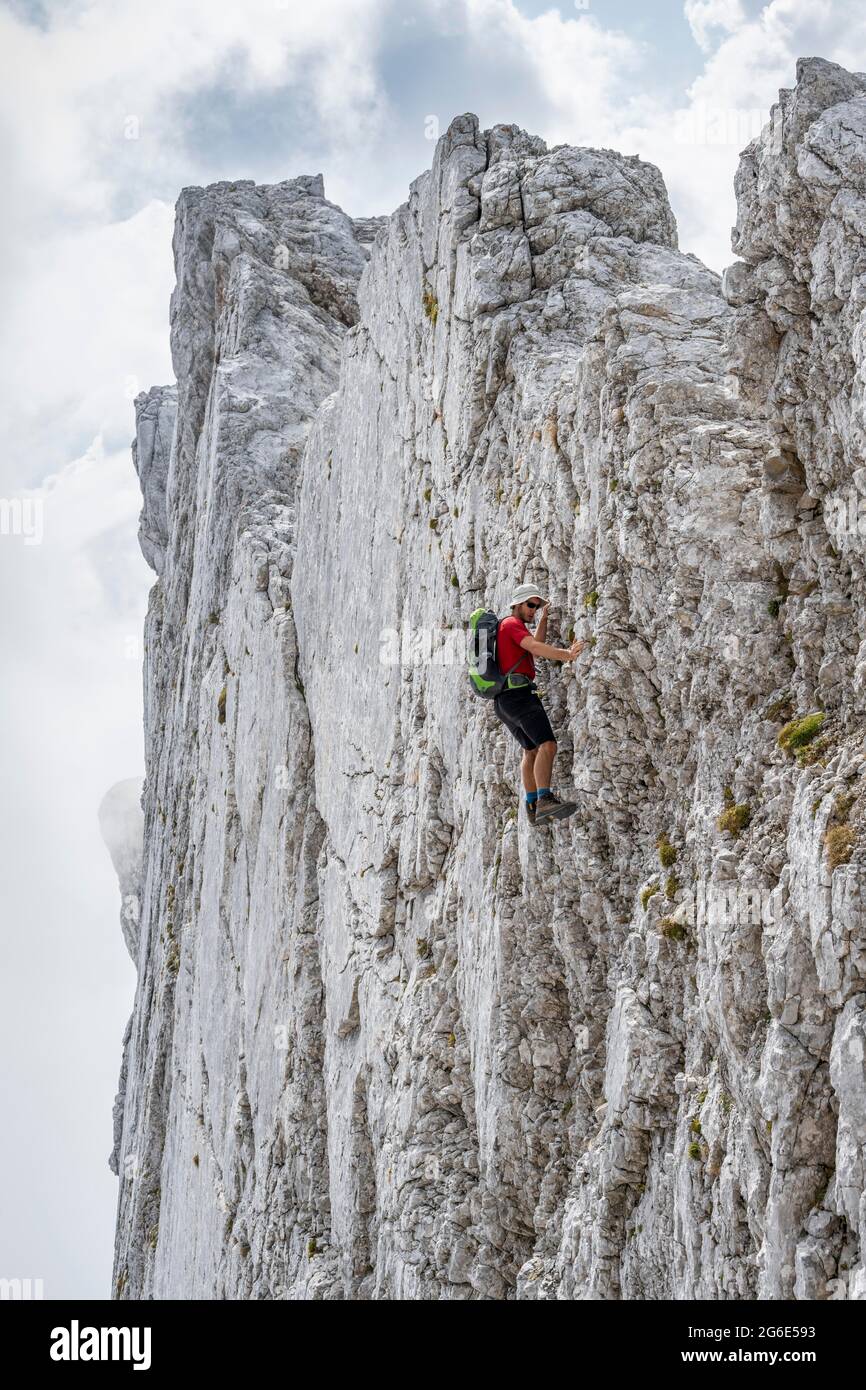 Young man climbing a vertical rock face without a rope, rocky mountains ...