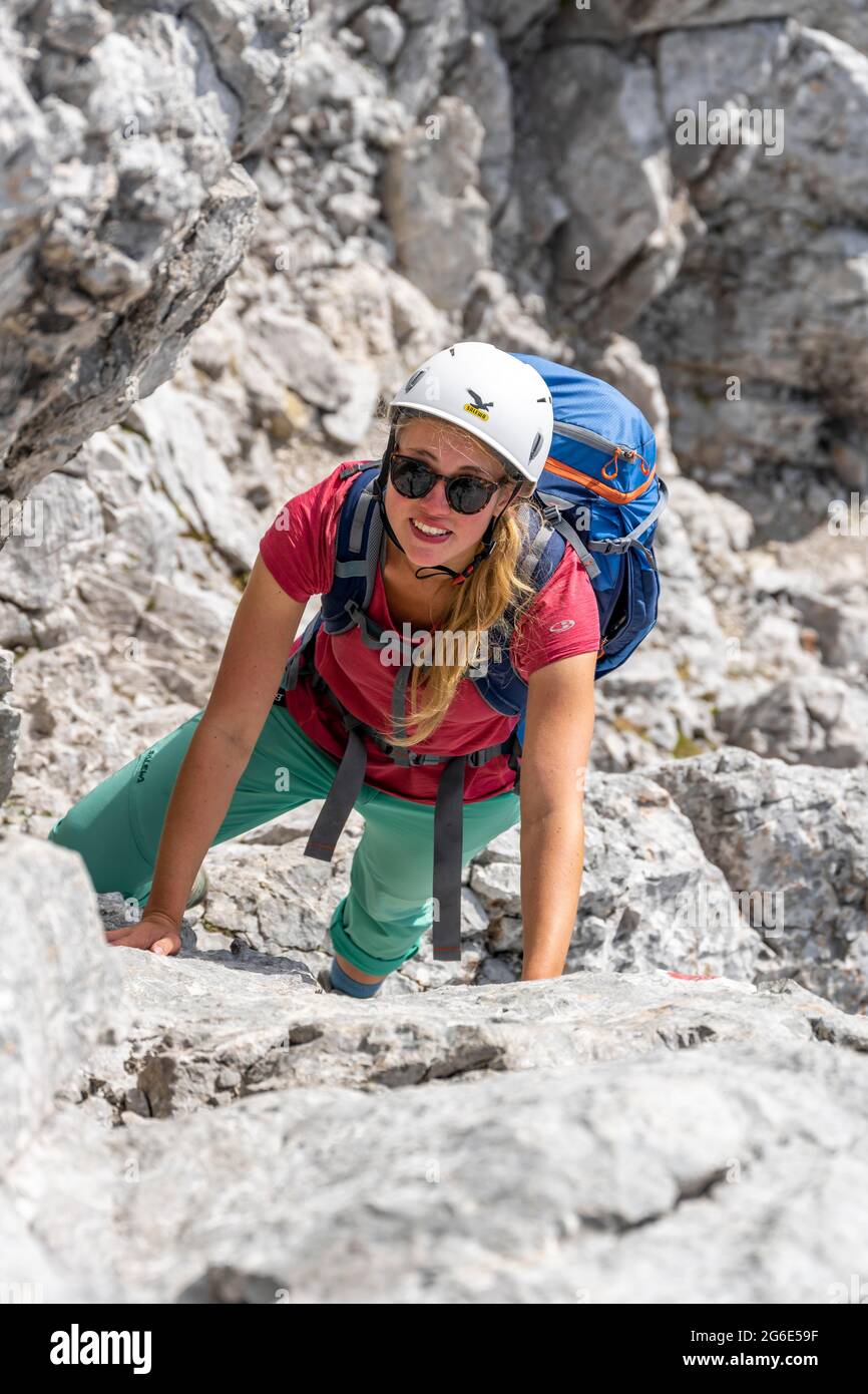 Young female hiker climbing with helmet, rocky mountains and scree ...