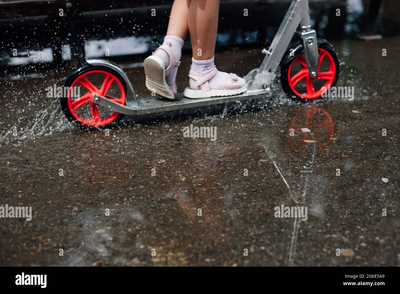 macro details the legs of a girl in summer shoes ride through a puddle ...