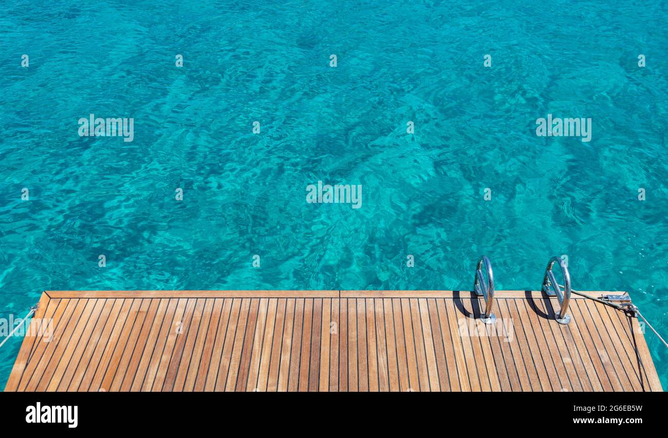 Yacht stern deck, teak wood and metal ladders, turquoise blue sea water ...