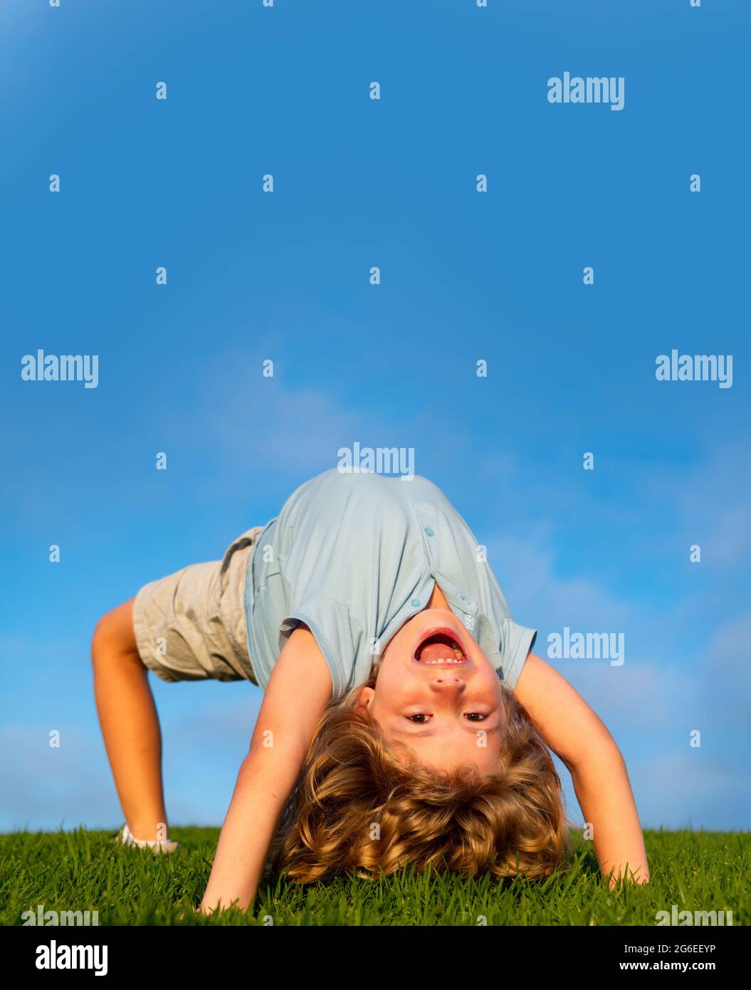 Happy child standing upside down on green grass. Laughing kid boy ...