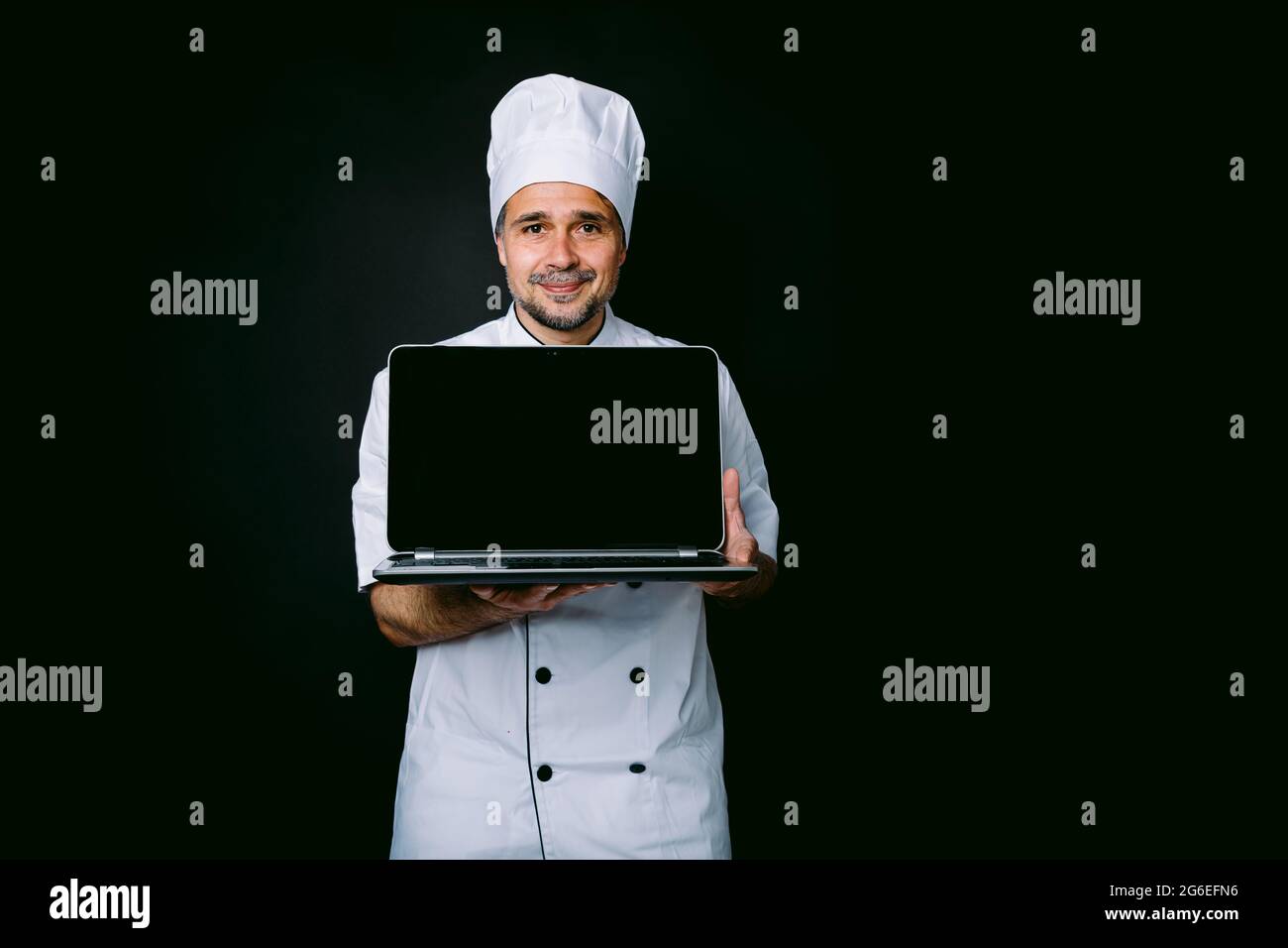 Chef cook wearing cooking jacket and hat, holding a laptop and showing ...