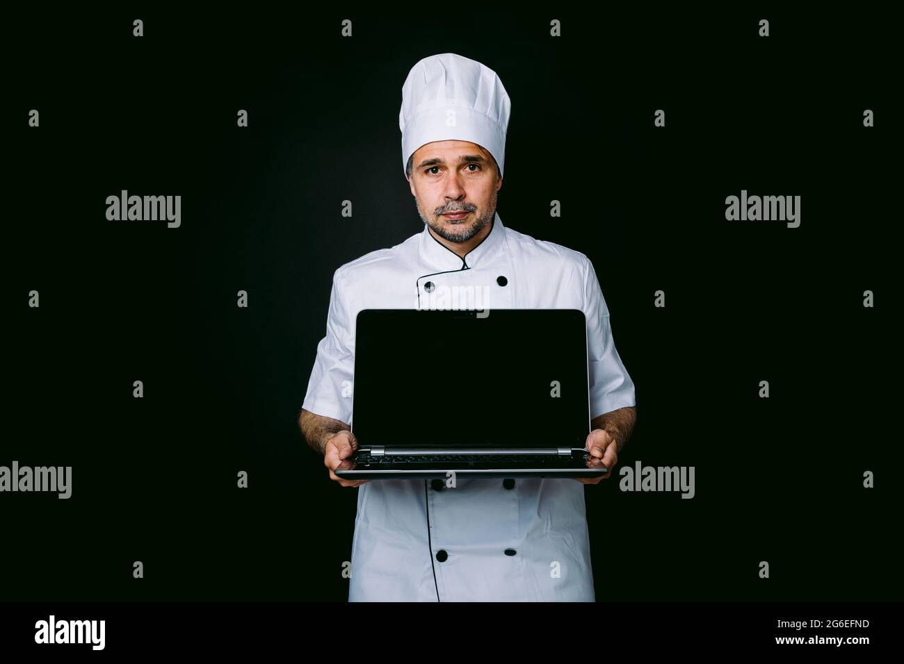 Chef cook wearing cooking jacket and hat, holding a laptop and showing ...