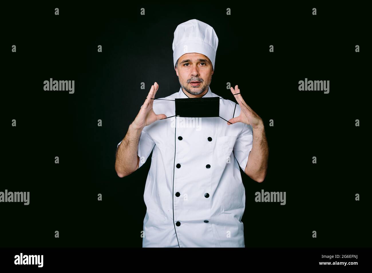 Chef cook wearing cooking jacket and hat, putting on a black mask, on ...