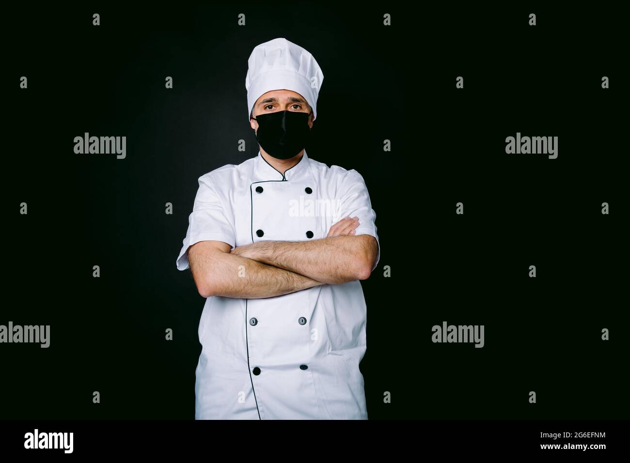 Chef cook wearing kitchen jacket and hat, with black mask, crossing ...