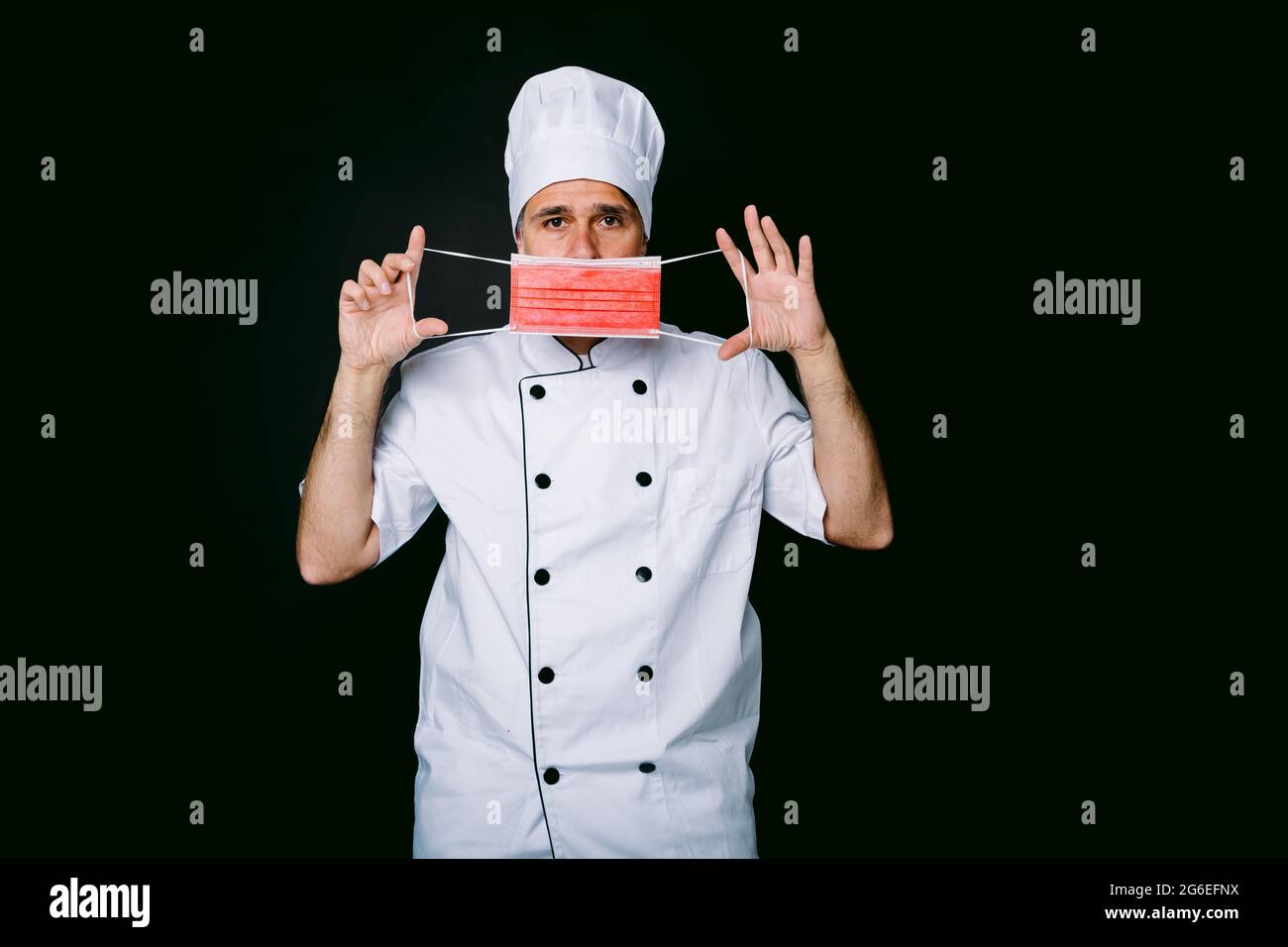 Chef cook wearing cooking jacket and hat, putting on a red mask, on ...