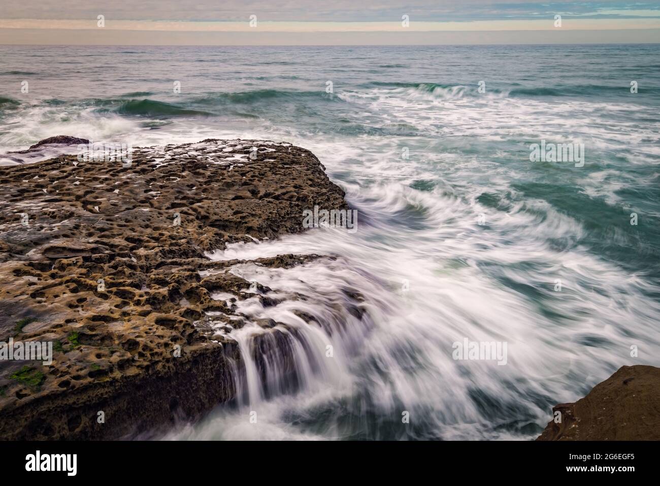 Long exposure surf crashing against beach bluffs on a cloudy day Stock ...