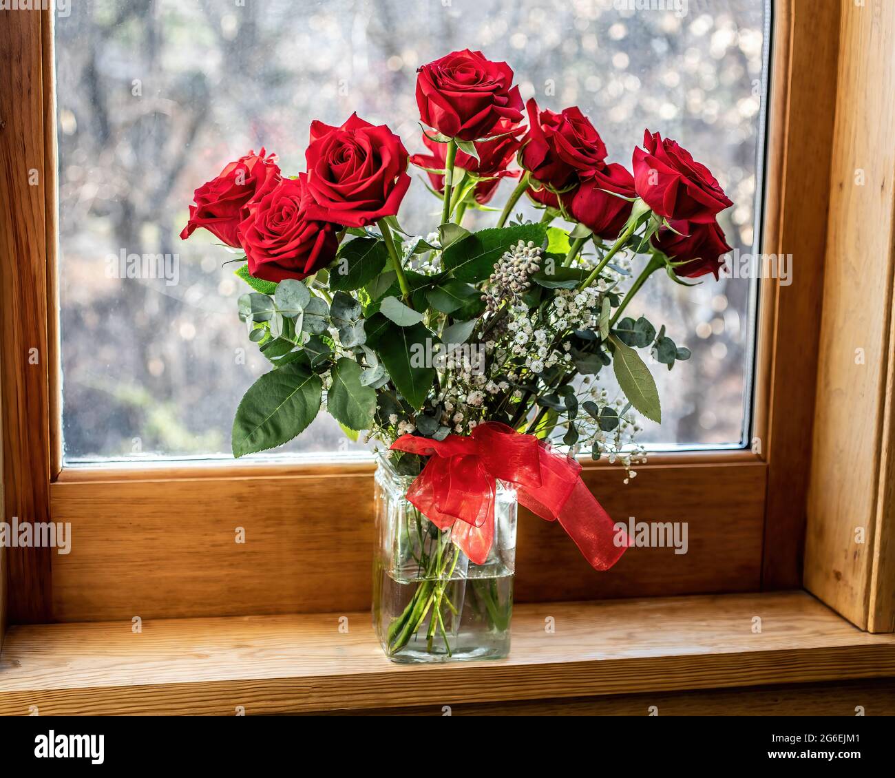 Pretty red roses in a glass vase with a red bow in front of a window ...