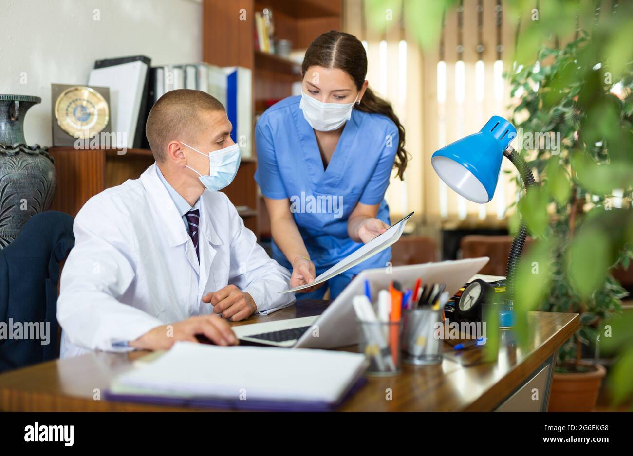 Head in protective mask gives task to assistant at office Stock Photo ...