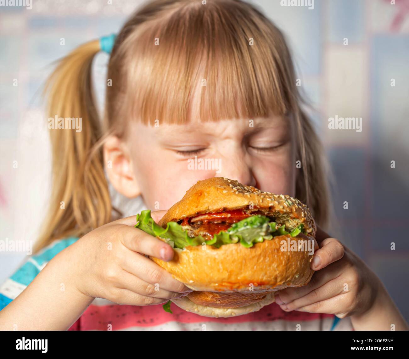 baby eating a big fast food hamburger with a lot of calories. The ...