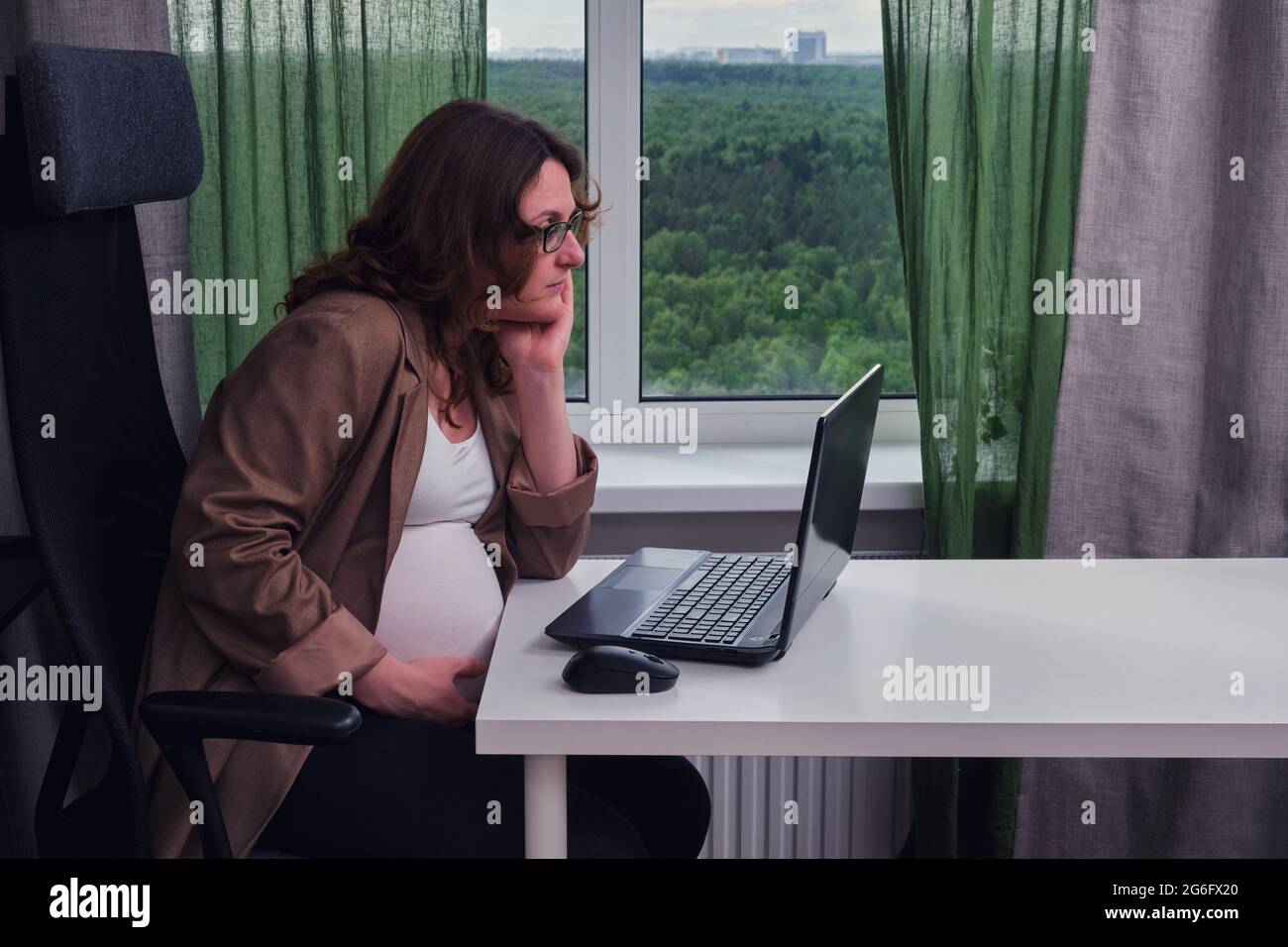 A pregnant woman with a laptop in her home office is crying and ...