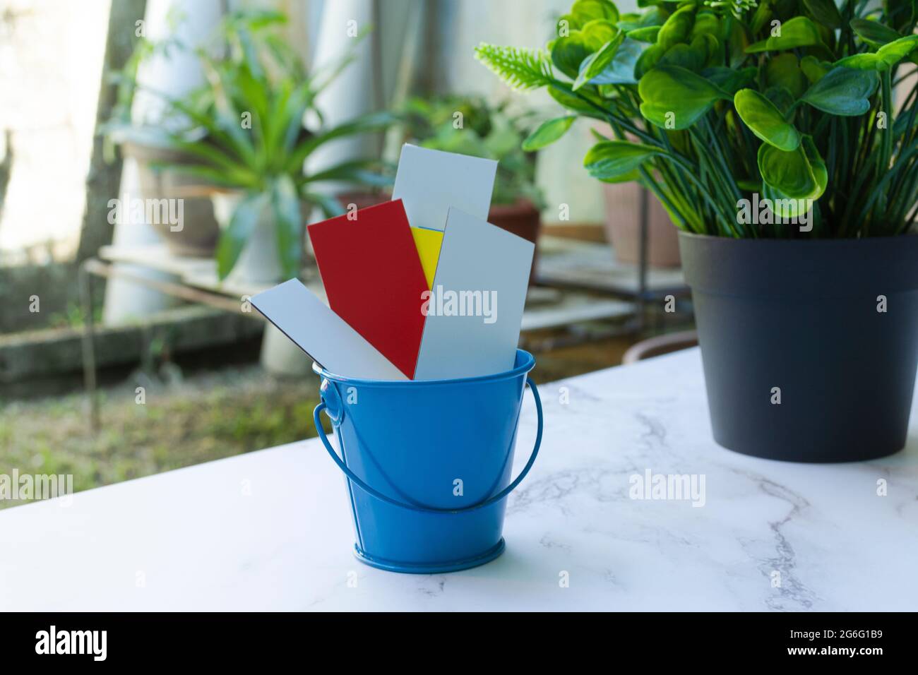 Colorful paper inside of a blue bucket on a white table with garden ...