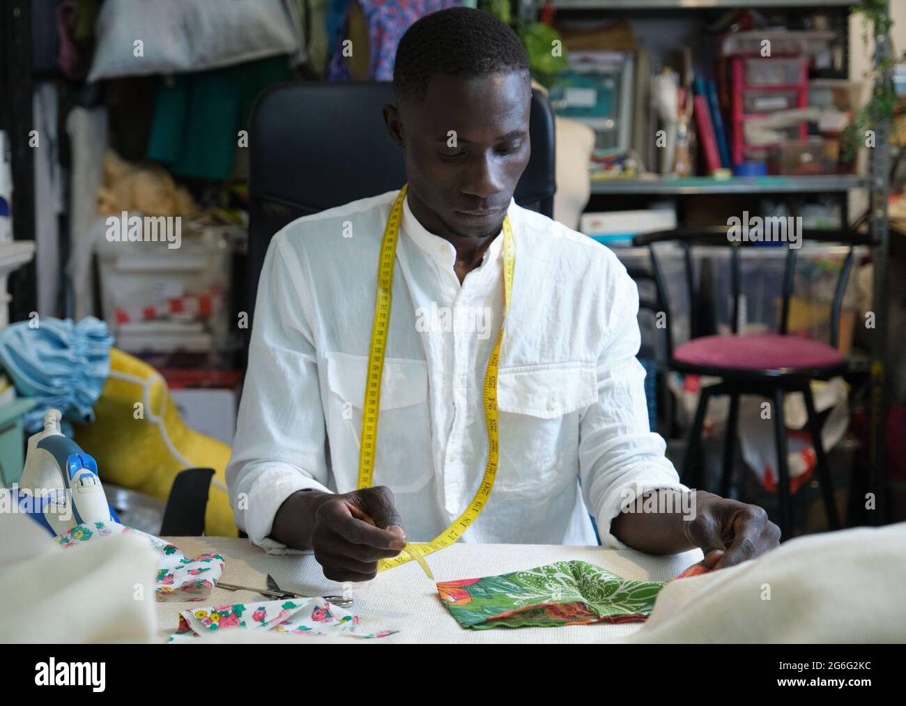 A tailor measuring fabric in his sewing shop using a measure tape ...