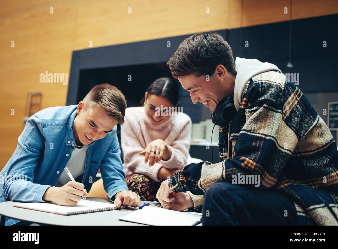 Young man writing notes while studying with friends in high school ...