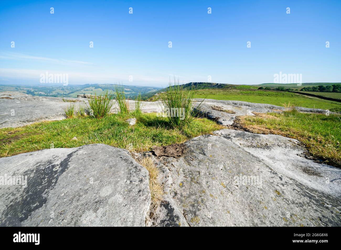 Grass begins to grow over weathered lichen covered gritstone slabs on ...