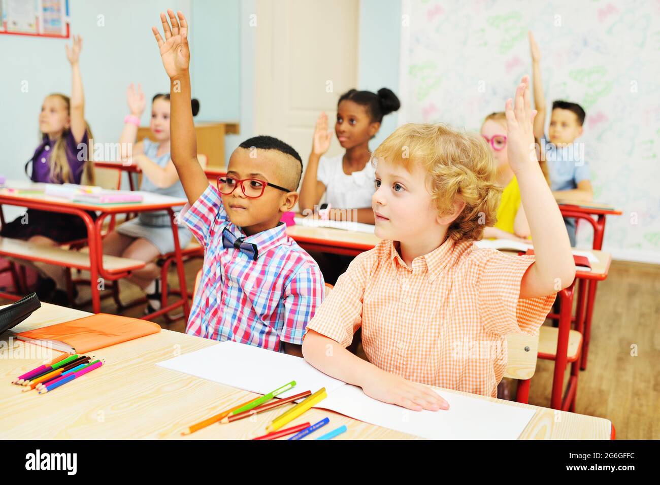 two little school boys pull their hand up to answer a teacher's ...
