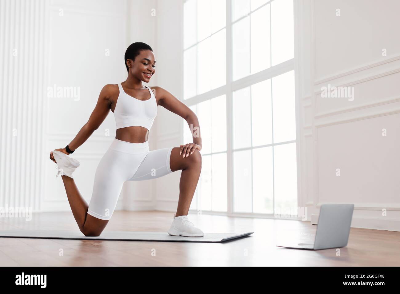 Cheerful black woman stretching leg muscles using pc Stock Photo - Alamy