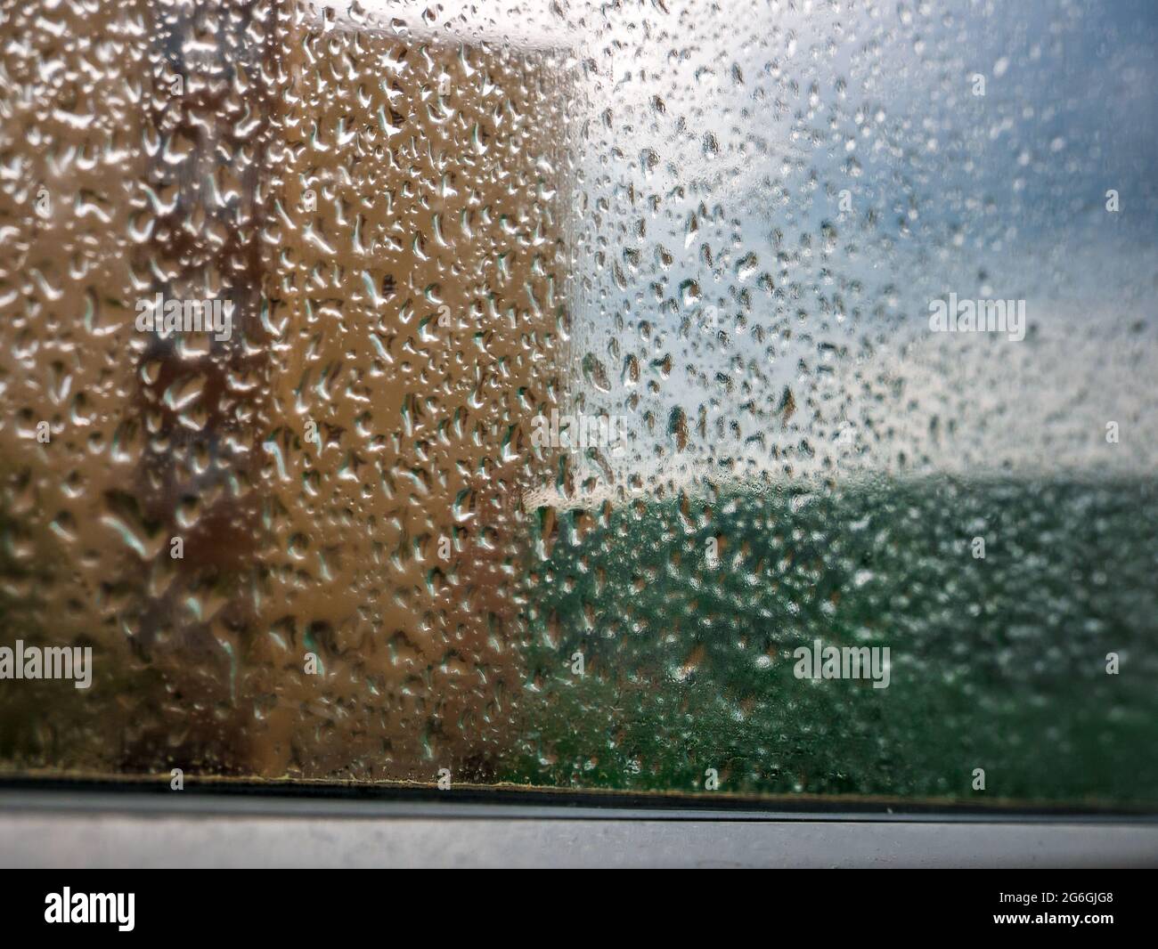 Rain drops on the window glass. Blurred background with house, greenery ...