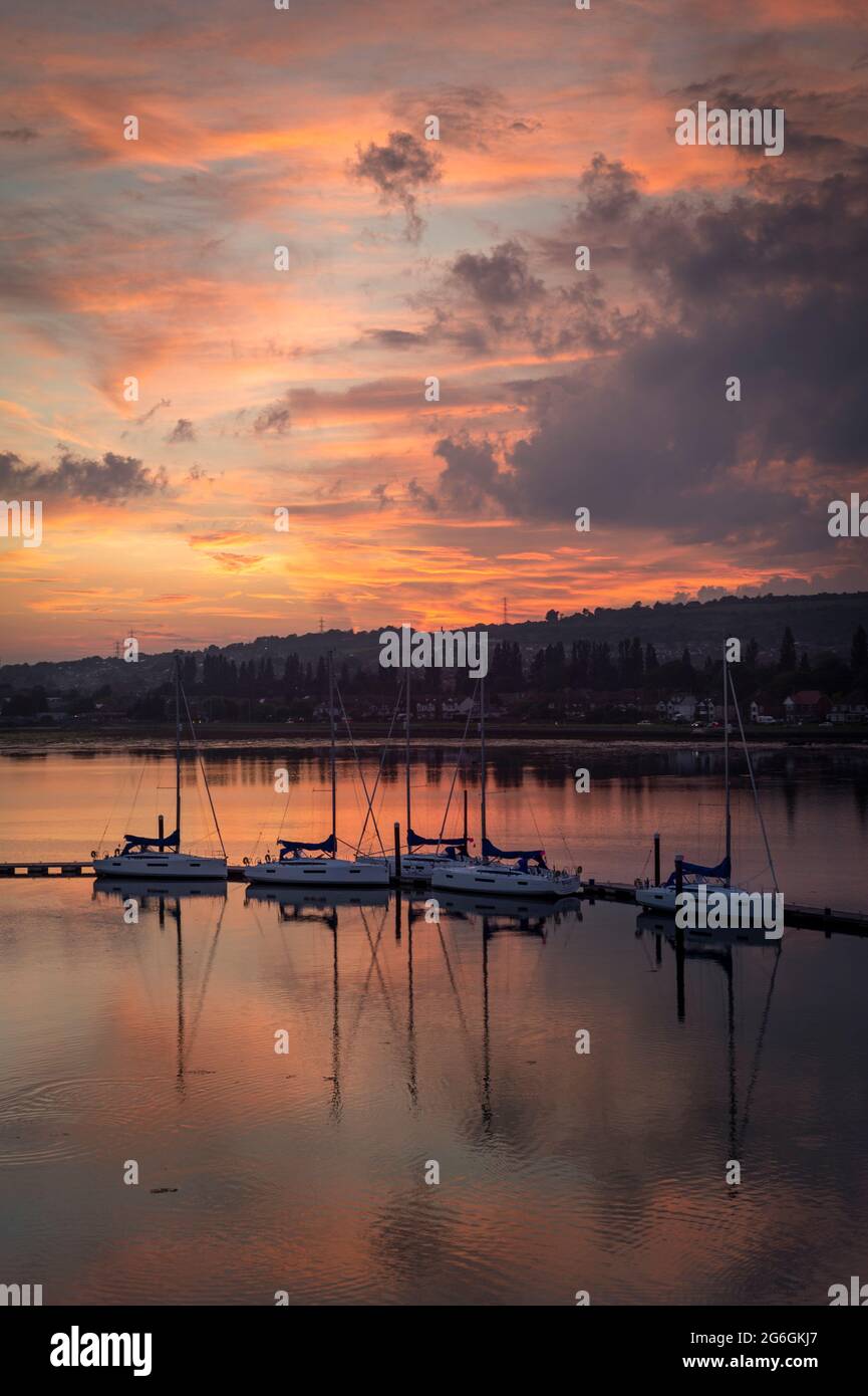 Sailing yachts moored on a pontoon at sunset in a peaceful harbour ...