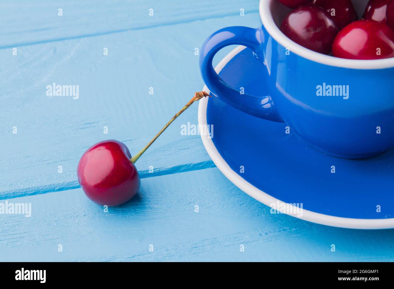 Shiny cherry and blue cup on wooden desk surface Stock Photo - Alamy