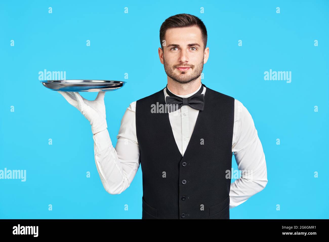 Attractive young waiter holding empty silver tray over blue background ...