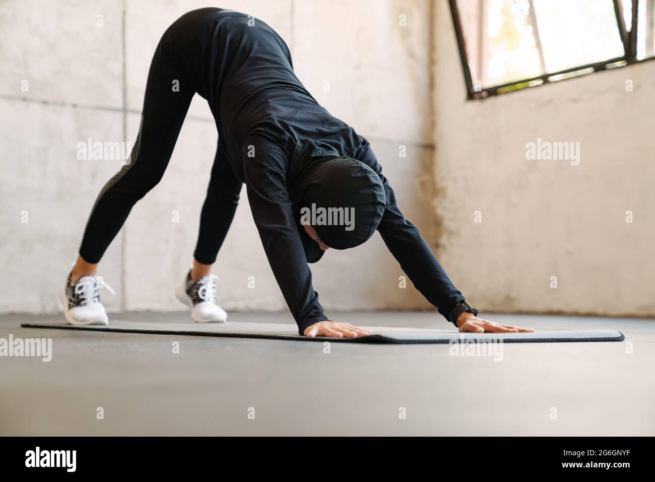 Young muslim woman in hijab doing exercise during yoga practice indoors ...