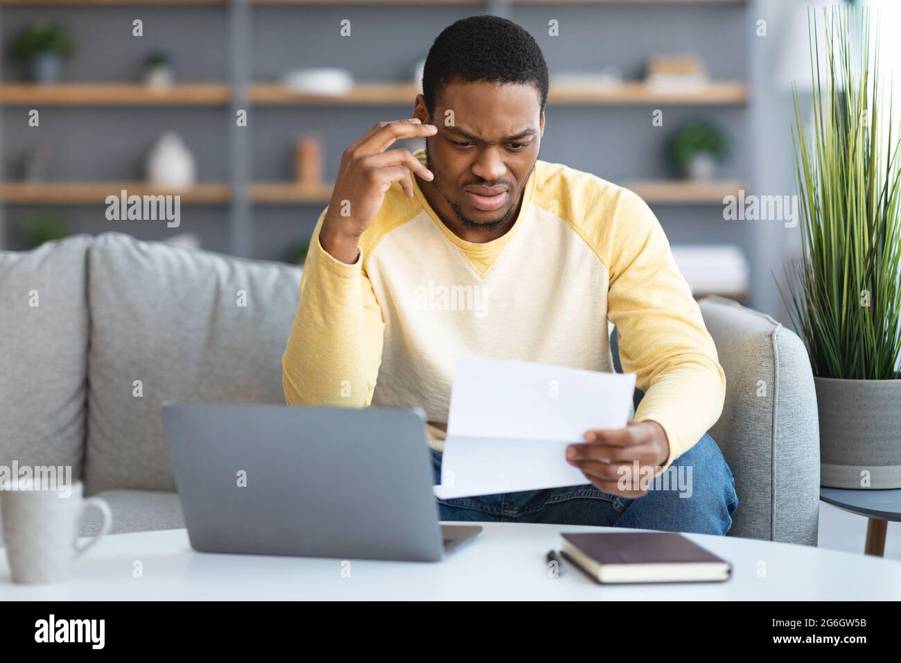 Confused black man sitting in front of laptop, holding papers Stock ...