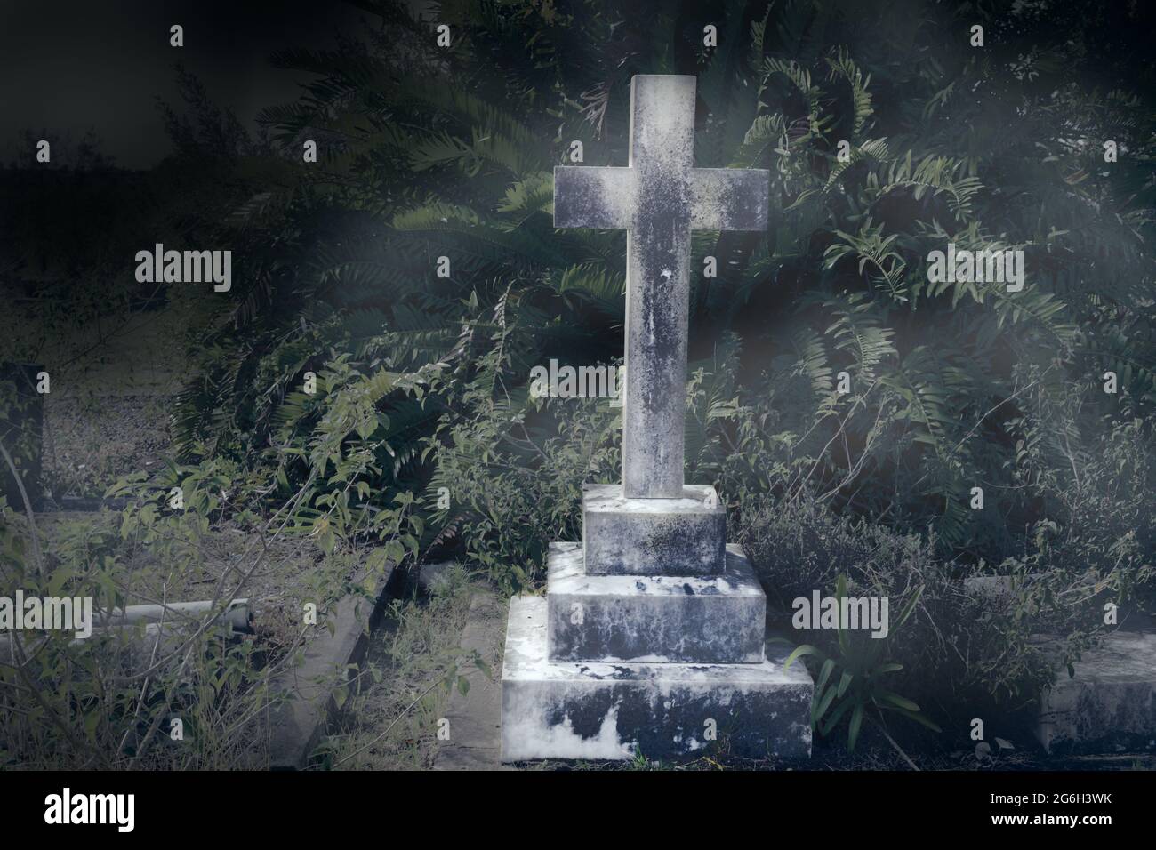 Tombstone in rundown graveyard with tropical plants and vines - cross ...