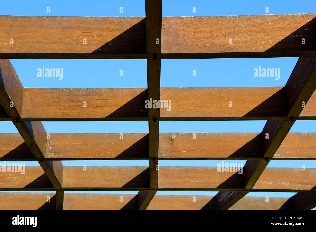 Looking up through a lattice wooden grid with a clear blue sky on a ...