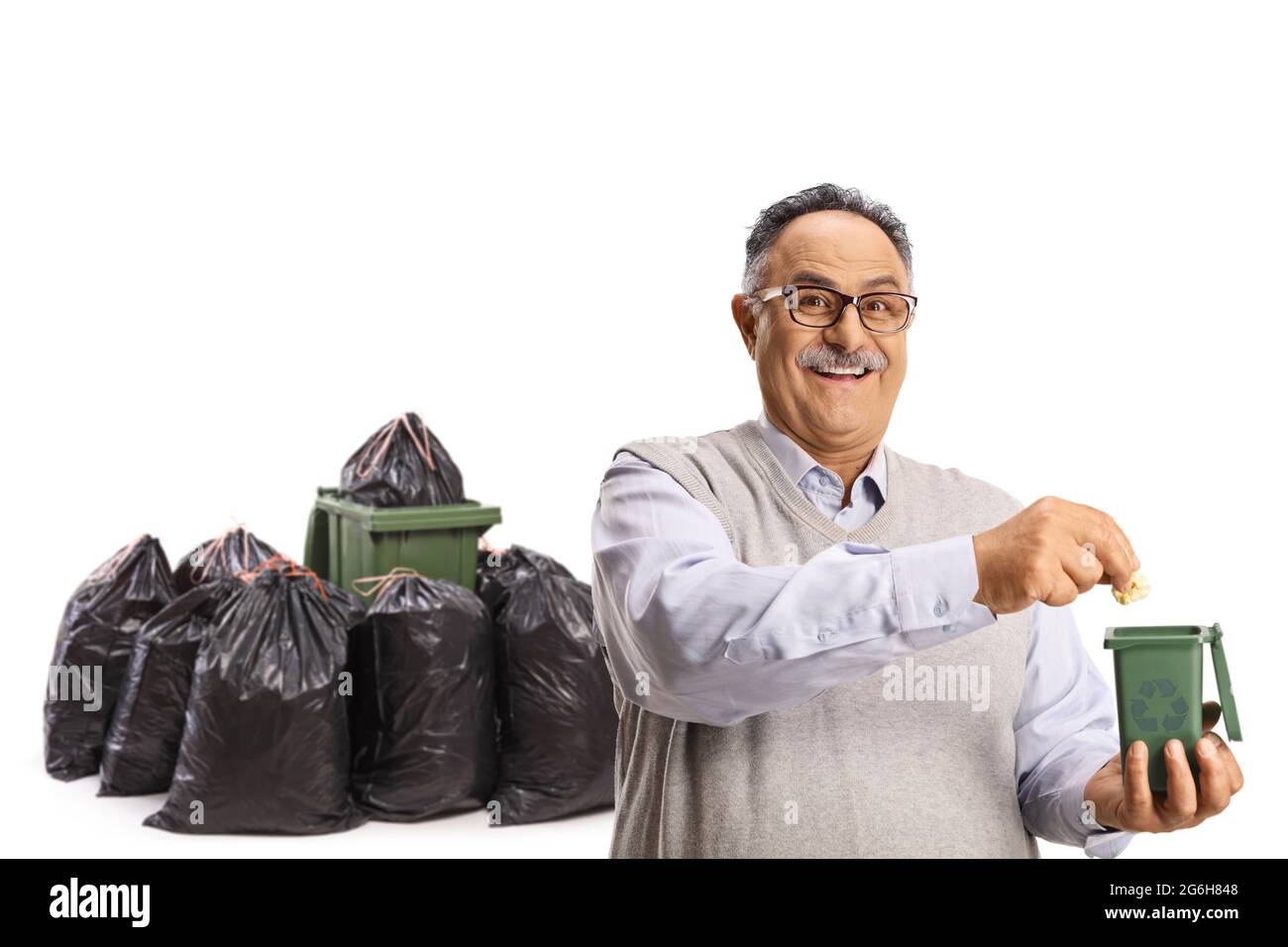 Mature man throwing paper in a small green bin in front of a pile of ...