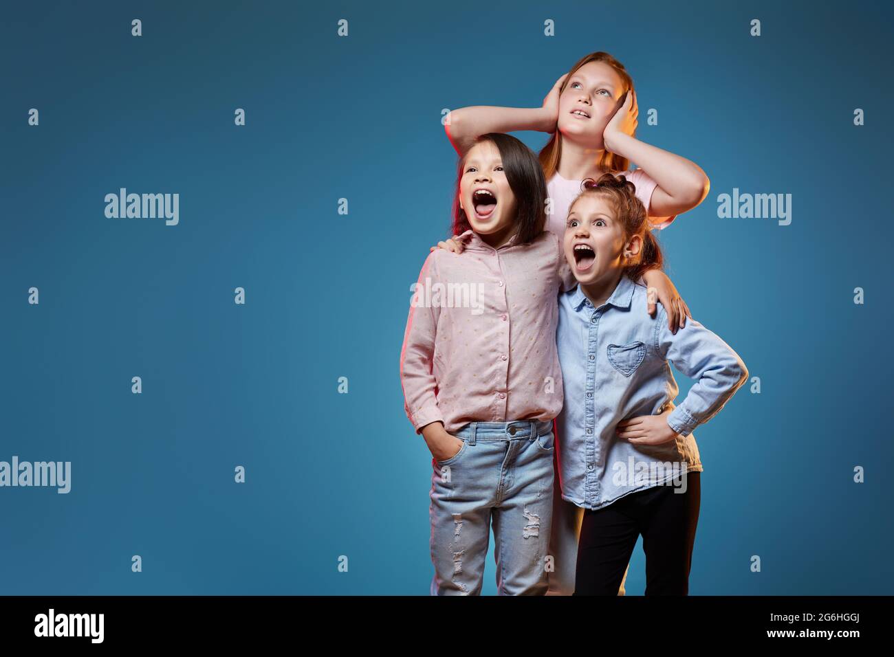 three kids girls standing together on blue background Stock Photo - Alamy