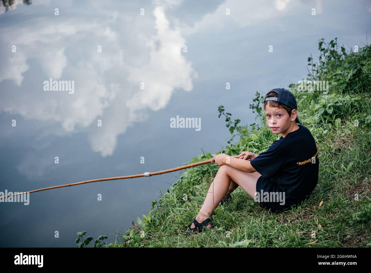 A boy holding a fishing rod and fishing in the lake, summer activities ...