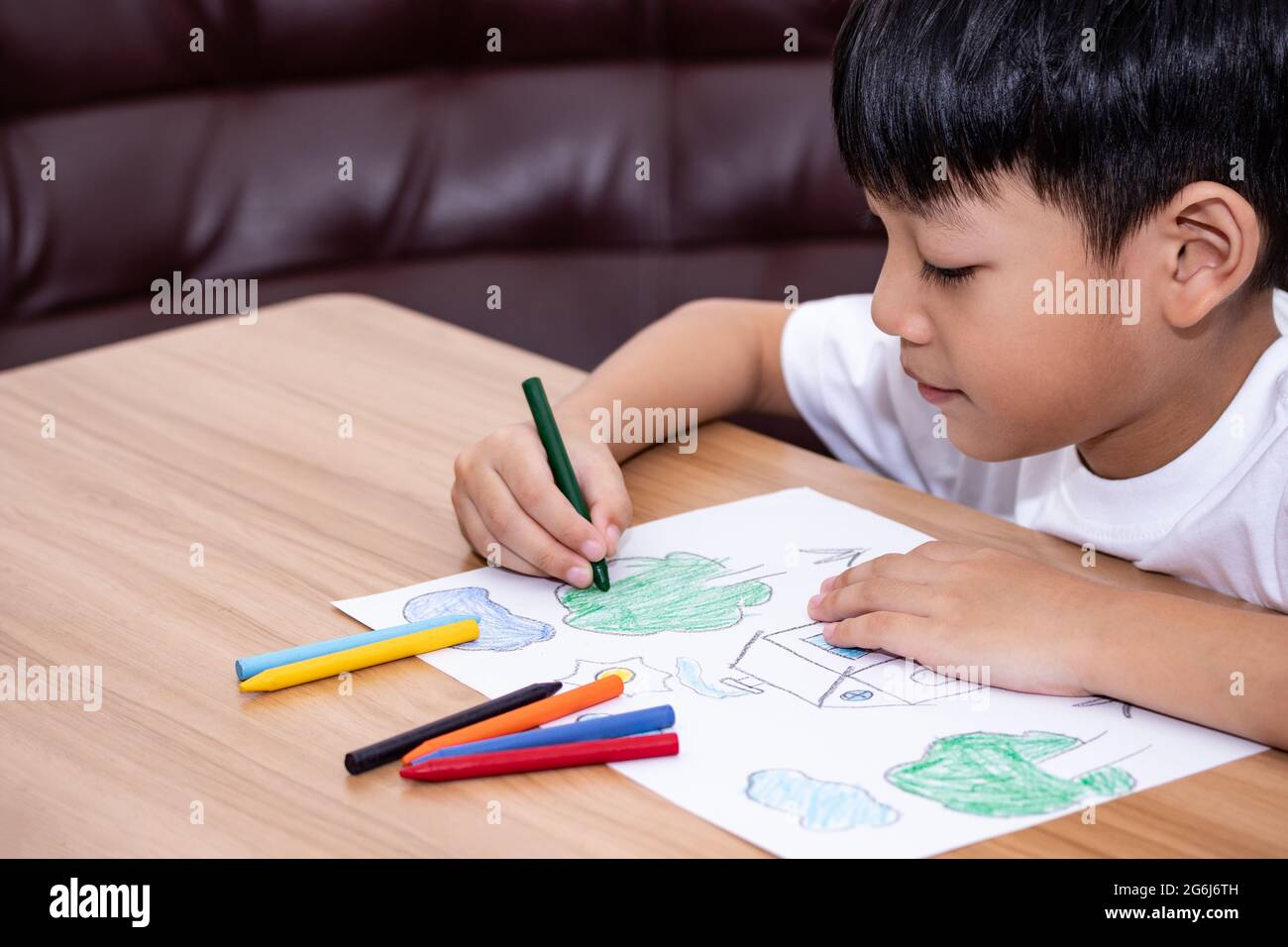 A little Asian boy is happily drawing a house with crayons is a ...