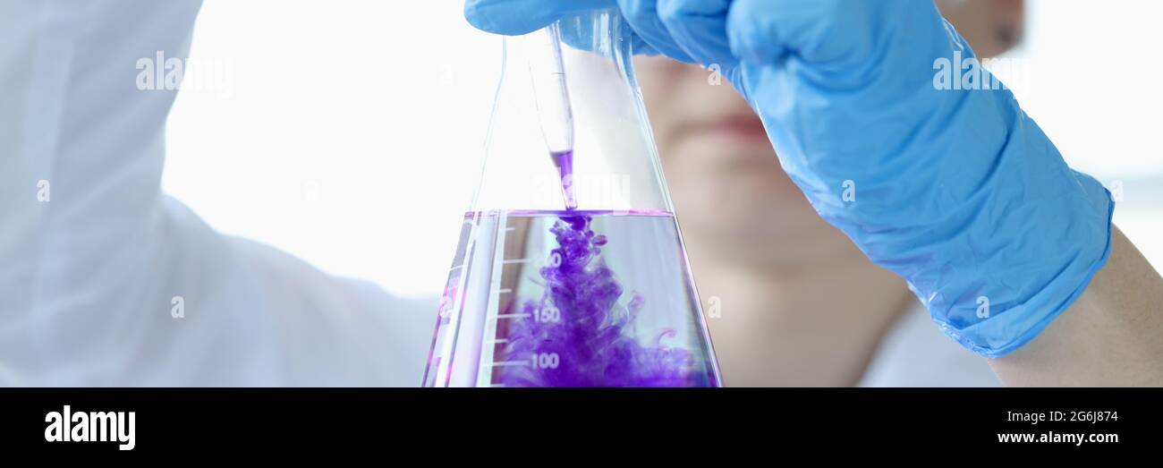 Woman scientist dripping purple liquid into flask with solvent closeup ...