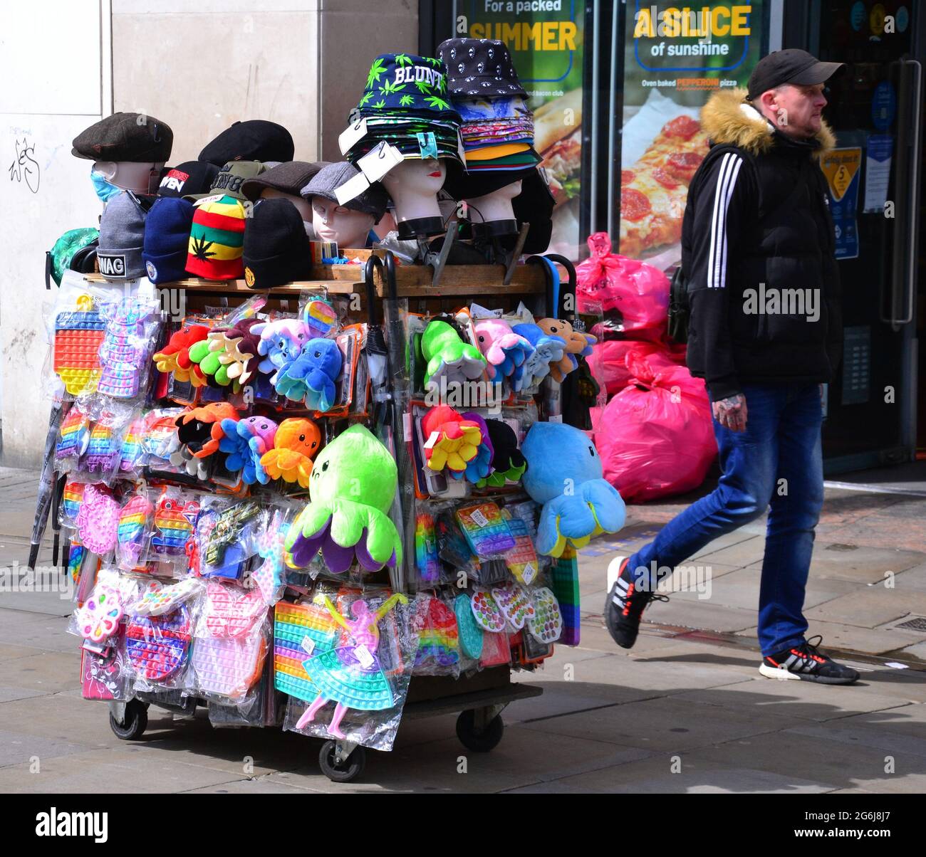 Man passes a trolley selling caps and toys in city centre Manchester ...
