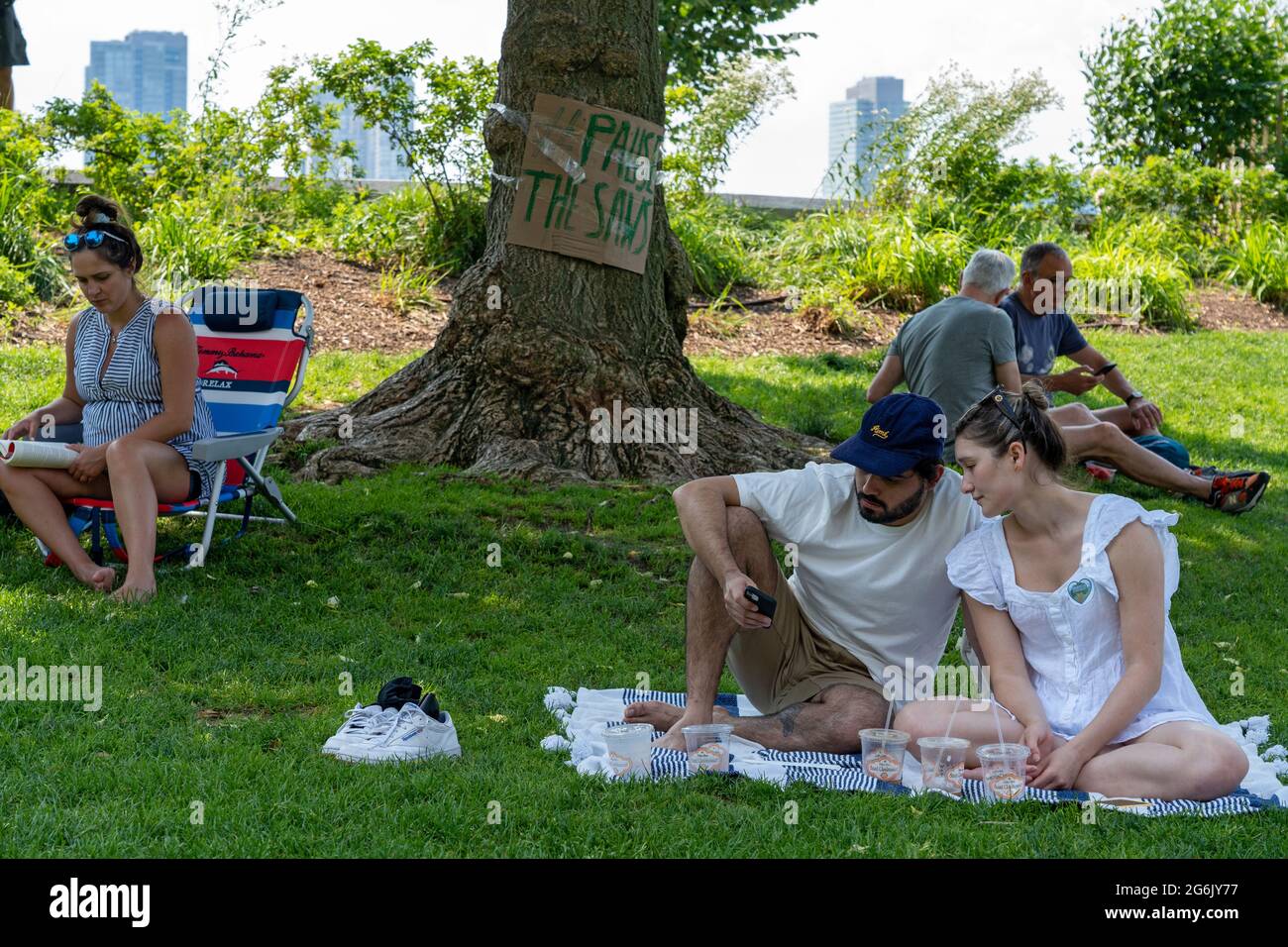 NEW YORK, NY – JULY 05: People rest in the shade of a tree with a sign ...