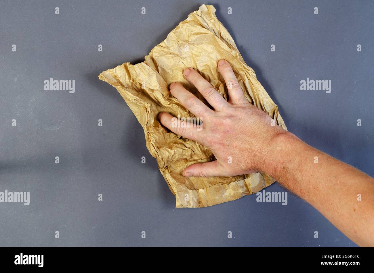 Man holding a dirty brown paper bag on a gray background. Hand crumples ...
