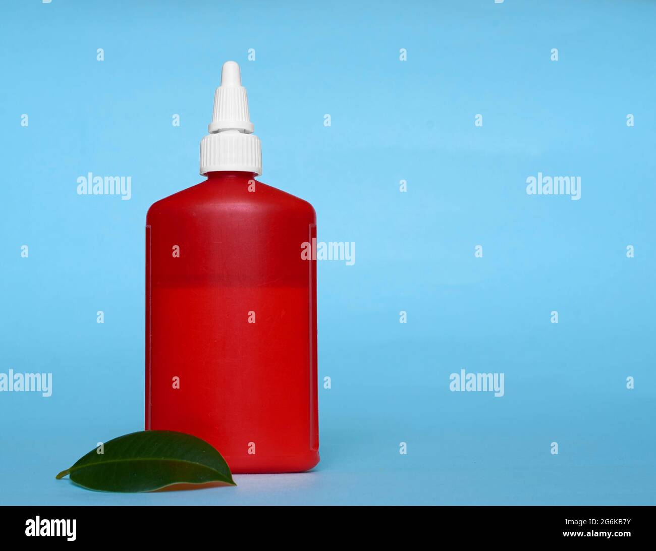 A red tube with a white cap and a green ficus leaf on a blue background ...