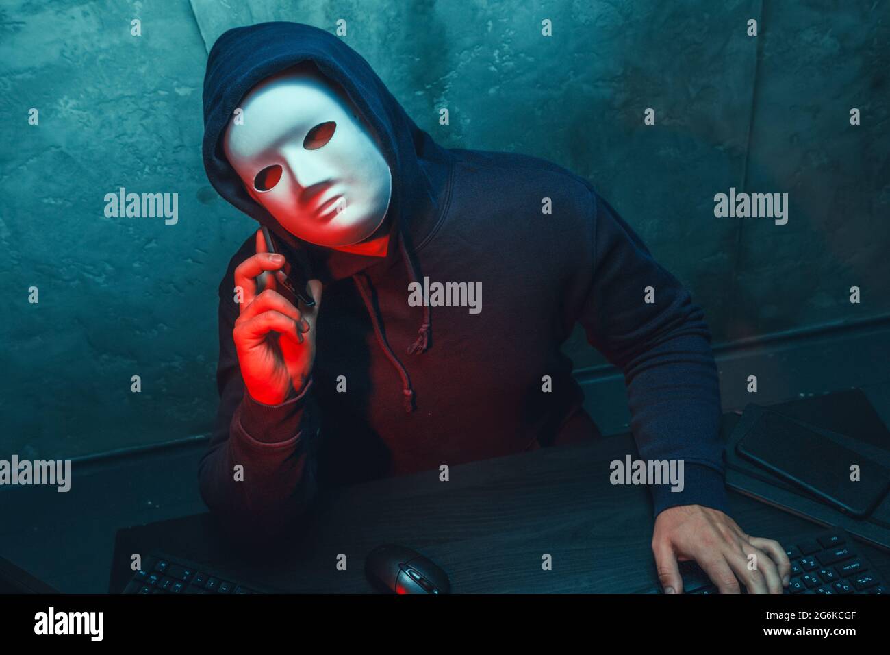 Anonymous hacker wearing face mask working on computer in dark room ...