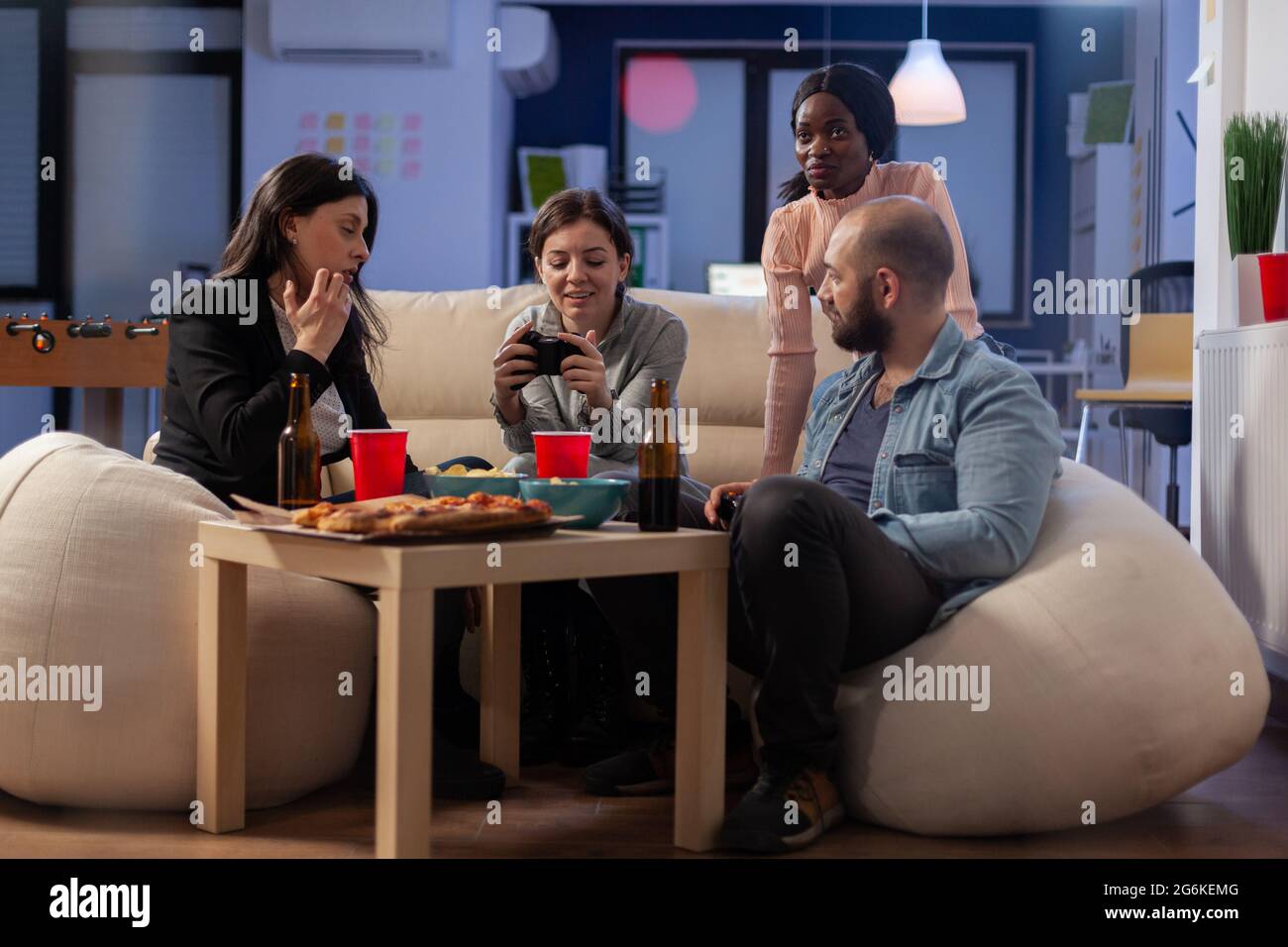 Multi ethnic group of coworkers play game on console while holding ...