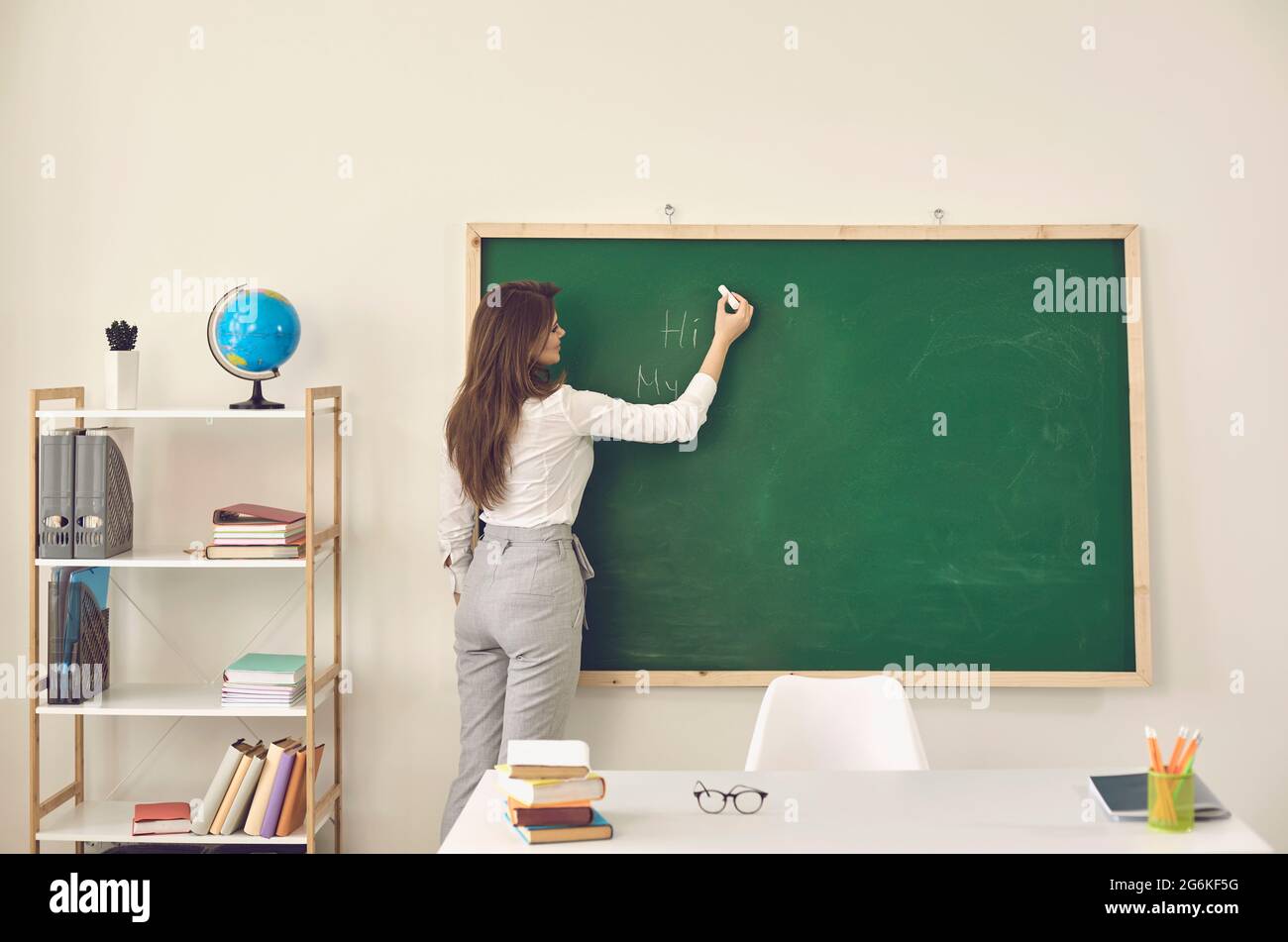 Back view. Young woman teacher writes on chalkboard in high school ...