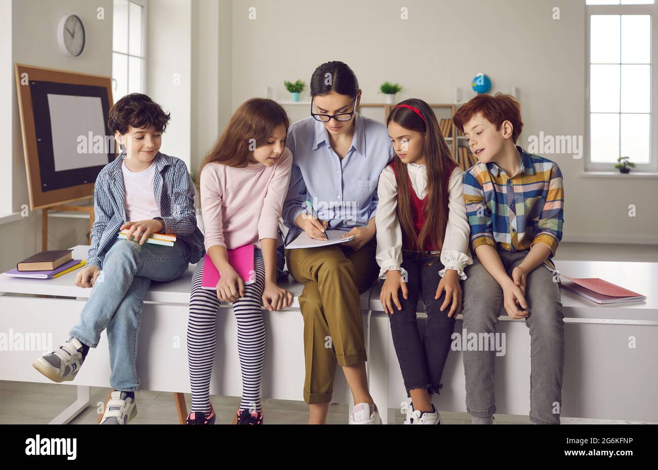 Kind female teacher checking pupils school lesson homework in classroom ...