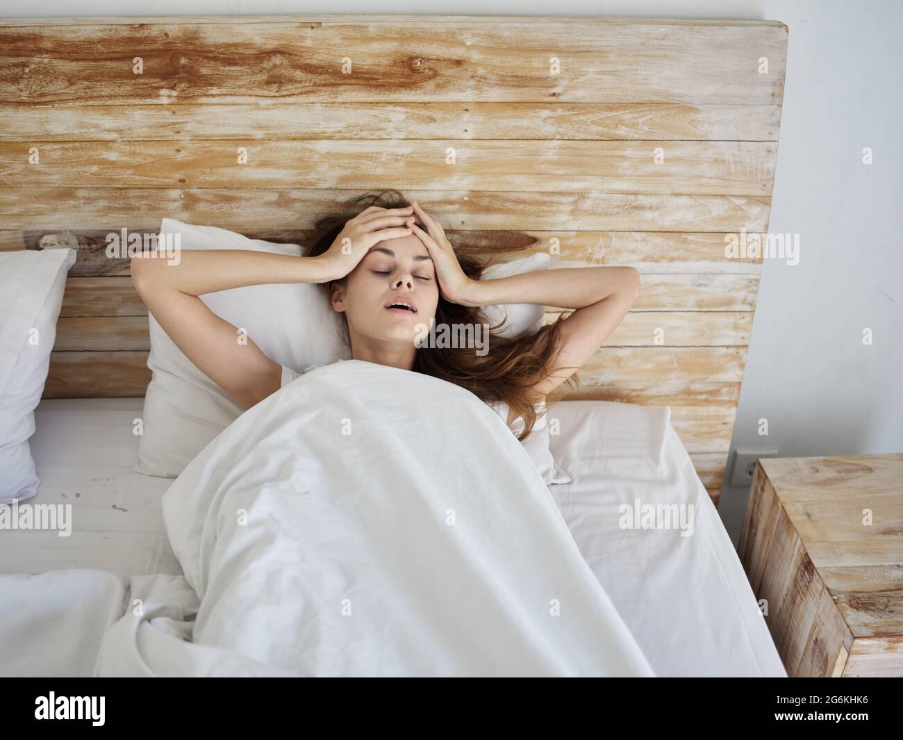 Woman Lies In Bed Under The Covers And Holds Her Head Emotions Stock
