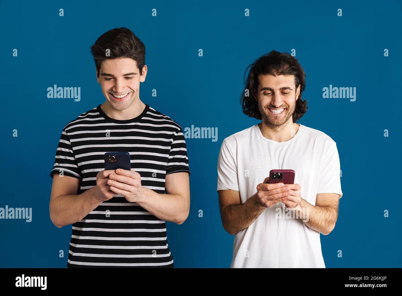 White happy two men smiling while using mobile phone isolated over blue ...