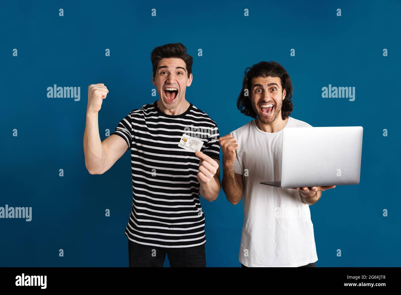Excited two men making winner gesture while holding laptop and credit ...