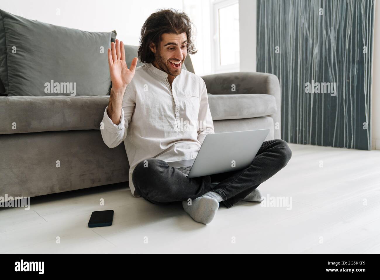 Smiling mid aged brunette turkish man sitting on a floor with laptop ...
